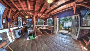 Interior rústico de cabana com cozinha, área de refeições e grandes portas de vidro deslizantes que dão para um pátio.