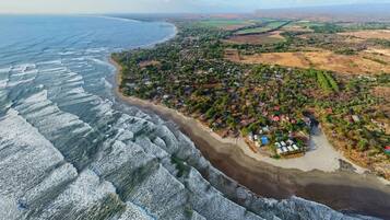 Vista aérea de uma vila costeira com praia, áreas residenciais e campos agrícolas.
