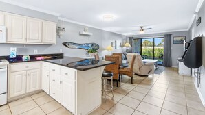 Cozinha moderna com armários brancos, bancada preta e área de refeições com cadeiras de vime e uma mesa.