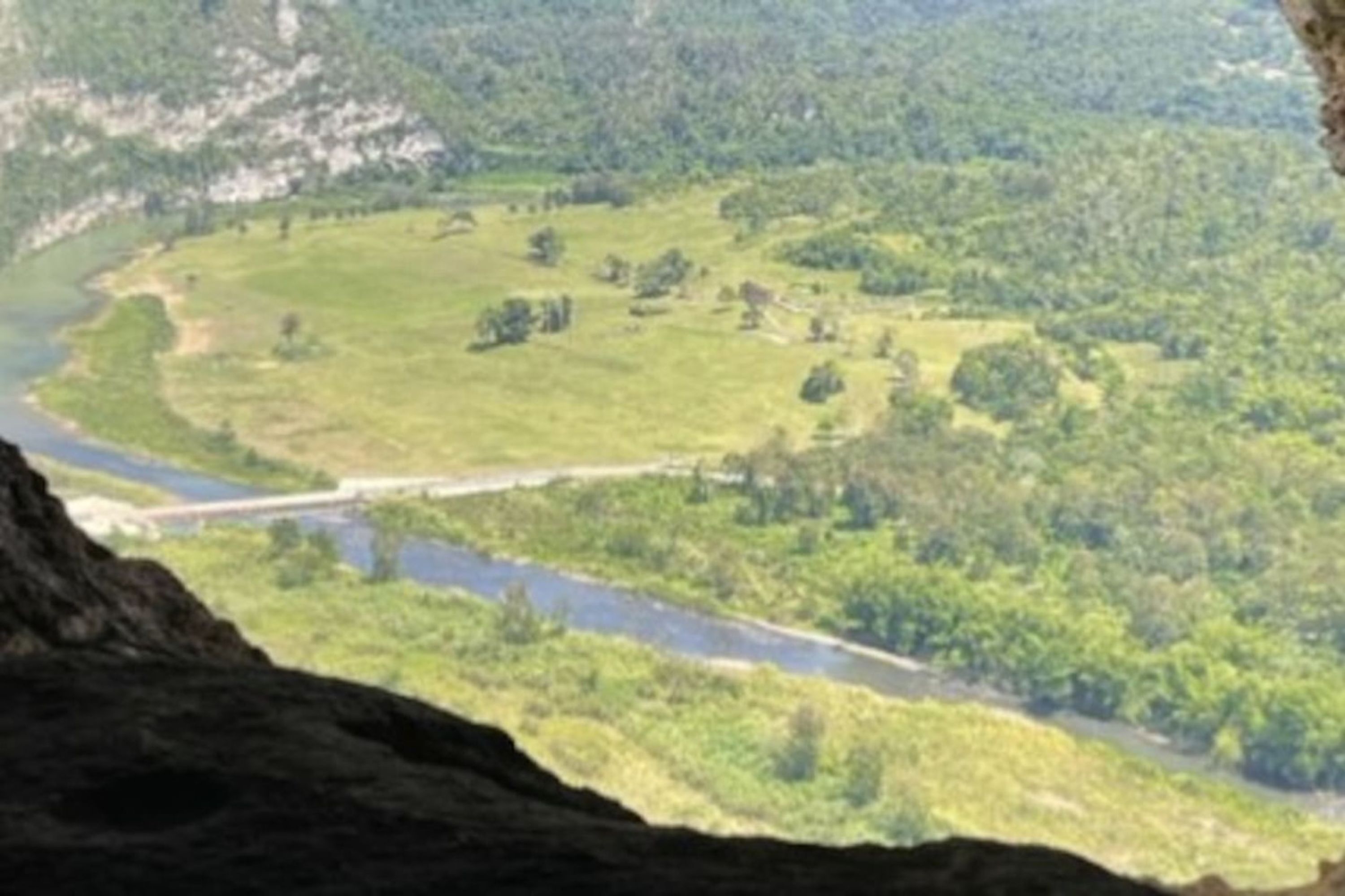 Um rio serpenteando por um vale, com colinas densamente arborizadas ao fundo.