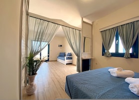 Quarto com cama, mesa de cabeceira, espelho, planta em vaso e vista para uma varanda.