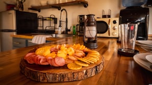 Uma tábua de corte de madeira com diversos petiscos e uma cafeteira em uma bancada de cozinha.