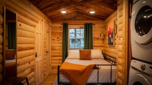 Quarto de cabana de tronco com uma cama, uma máquina de lavar e uma janela com cortinas.