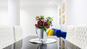 Mesa de jantar com um jarro de flores, cadeiras estofadas brancas e obra de arte na parede.