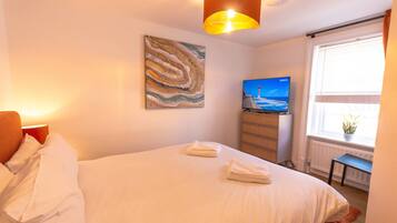 Quarto de hotel com cama, televisão, quadro e janela com persianas.