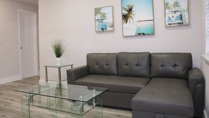 Uma sala de estar moderna com um sofá modular cinza, uma mesa de centro de vidro e três quadros pendurados na parede.