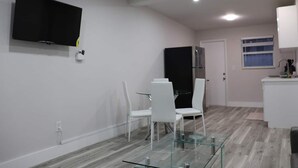 Uma cozinha moderna com armários brancos, geladeira preta e uma mesa de jantar de vidro com cadeiras brancas.