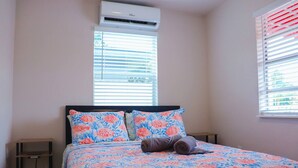 Quarto com cama, duas mesas de cabeceira, ar condicionado e janela com persianas.