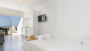 Quarto de hotel moderno com uma cama grande, uma TV fixada na parede e uma varanda com vista para o mar.