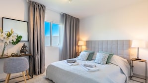 Quarto moderno com uma cama grande, mesas de cabeceira, escrivaninha e uma cadeira.