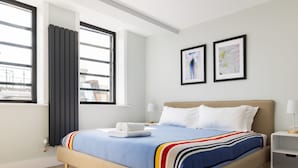 Quarto moderno com uma cama grande, uma mesa de cabeceira, duas fotos emolduradas na parede.