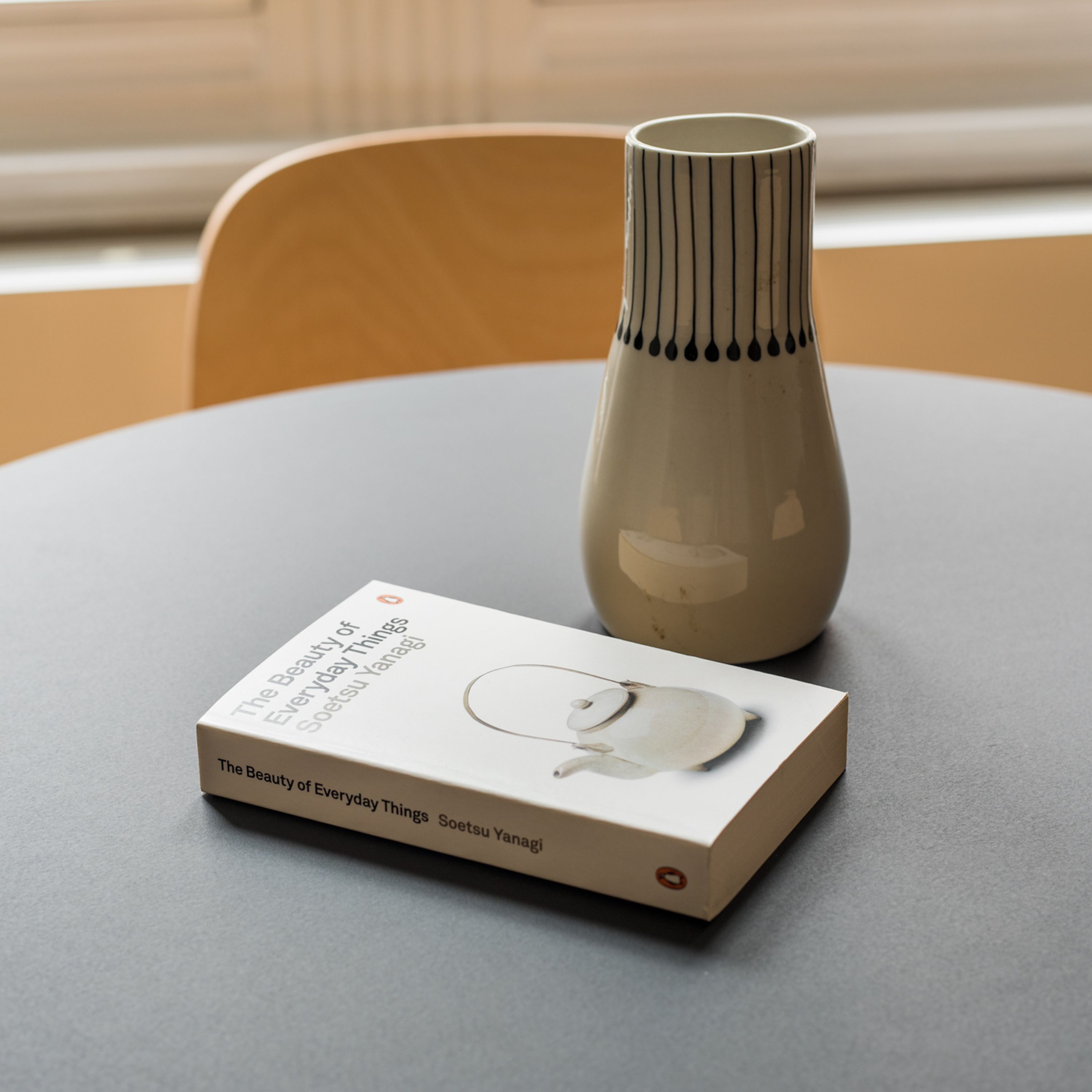 Um livro intitulado "A Beleza das Coisas Cotidianas" de Soetsu Yanagi sobre uma mesa ao lado de um vaso.