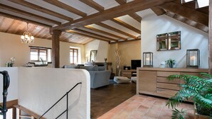 Uma sala de estar ampla com vigas de madeira, escada e uma grande janela.