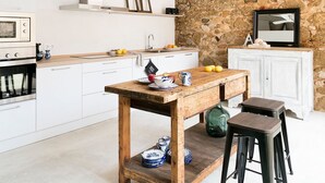 Uma cozinha moderna com armários brancos, uma mesa de madeira e uma parede de pedra.
