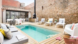 Uma área de piscina com espreguiçadeiras e uma mesa, rodeada por paredes de pedra e um telhado telhado.