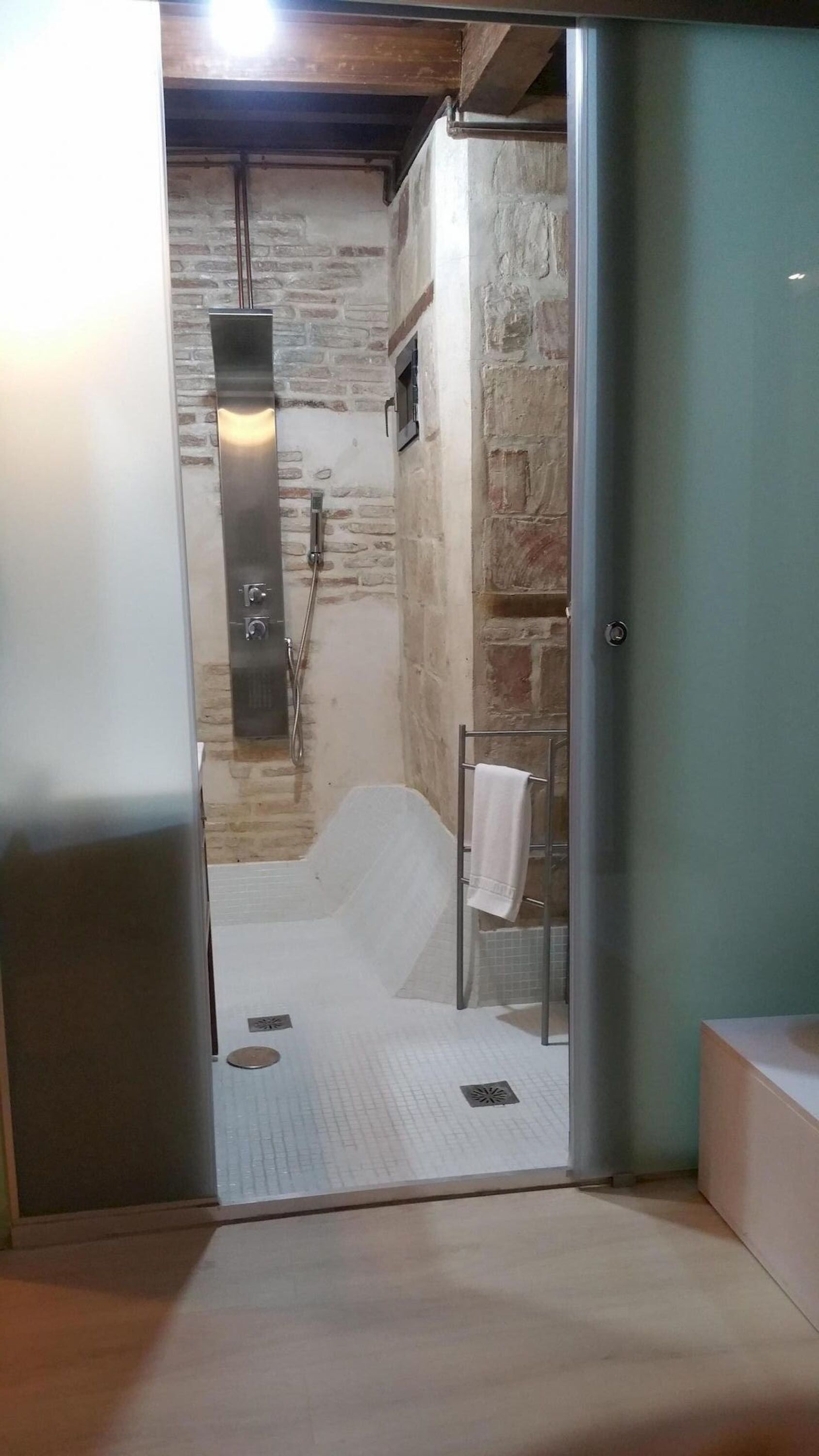 Quarto com parede de pedra, pia de metal e toalha branca pendurada em um suporte.