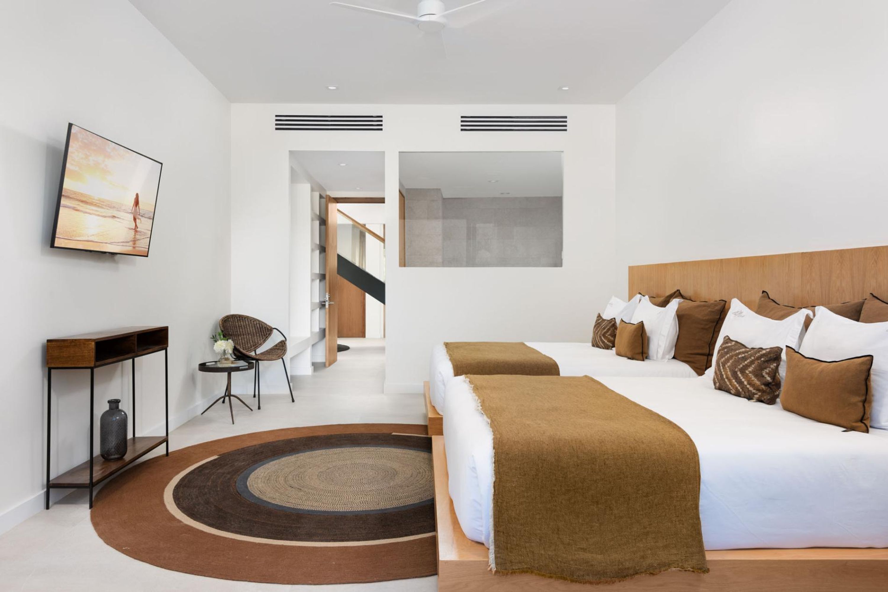 Quarto de hotel moderno com uma cama grande, um sofá pequeno, uma TV e vista para o corredor.