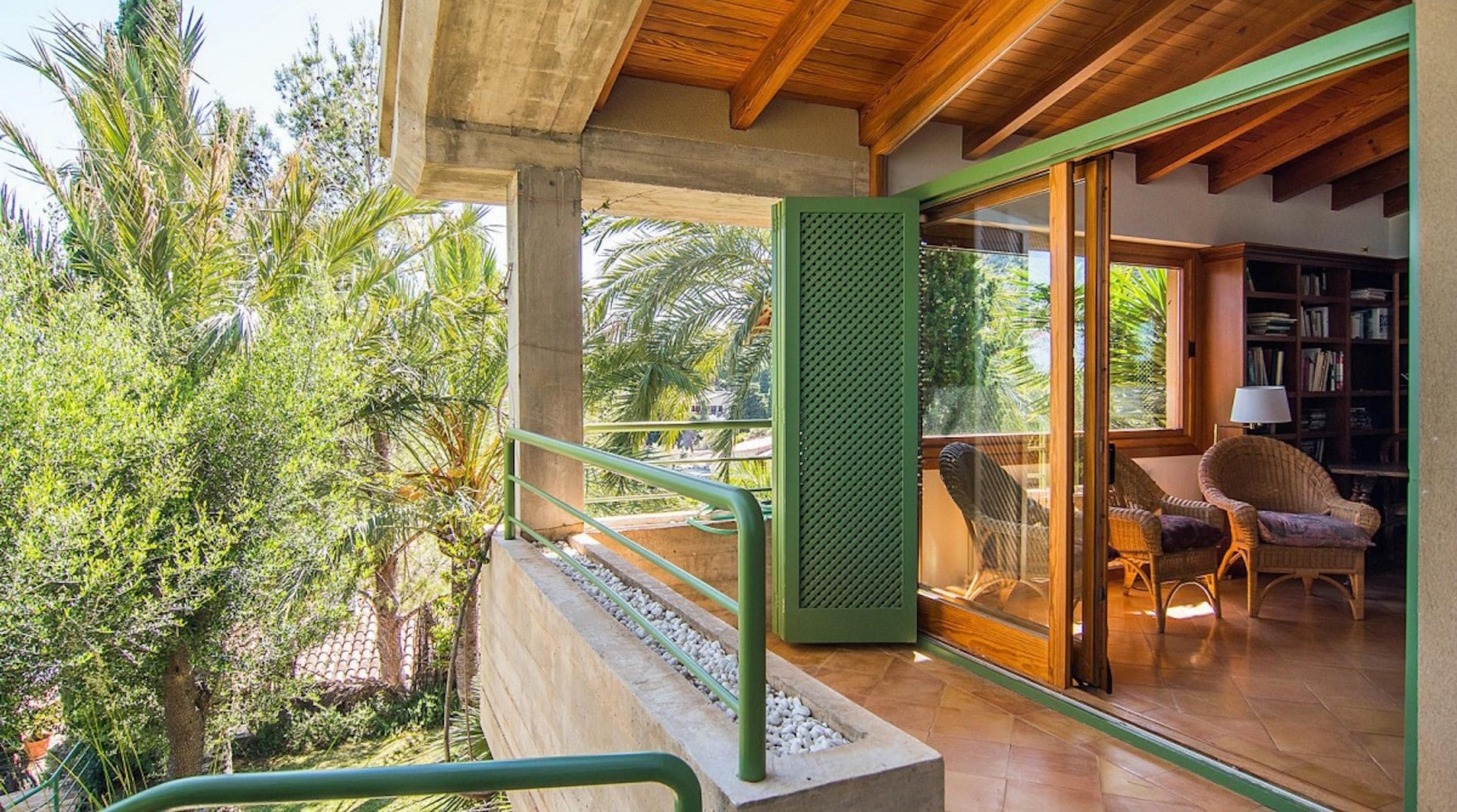 Varanda moderna ao ar livre com piso de concreto, guarda-corpo verde e vista para vegetação exuberante.