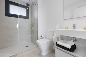 Uma casa de banho moderna com cabine de duche em vidro, sanita e lavatório com espelho.