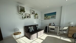 Uma sala de estar moderna com sofá, mesa de jantar e escrivaninha. Há prateleiras com plantas e um quadro na parede.