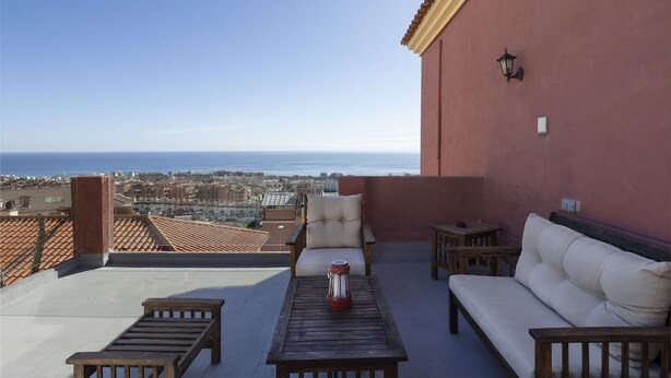 Terraço no telhado com vista para a cidade e o mar, mobiliado com sofá, cadeiras e mesa.