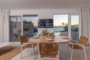 Uma área de refeições moderna com uma mesa redonda, quatro cadeiras de vime e uma televisão de tela plana na parede.