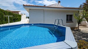Uma piscina com escada, um edifício branco com telhado em azulejo e um céu claro.