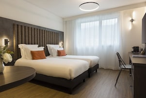 Quarto de hotel com duas camas, uma escrivaninha e uma cadeira.