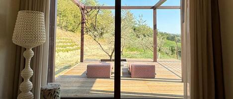 Quarto com uma grande porta de vidro deslizante que dá para um alpendre externo com dois pufes xadrez e vista para um vinhedo.