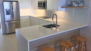 Uma cozinha moderna com eletrodomésticos de aço inoxidável, uma ilha central com banquetas e prateleiras de madeira acima da pia.
