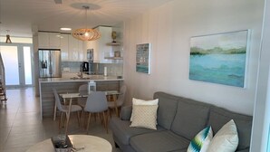 Uma sala de estar moderna com um sofá cinzento, uma mesa de centro redonda e uma área de jantar com mesa e cadeiras de vidro.
