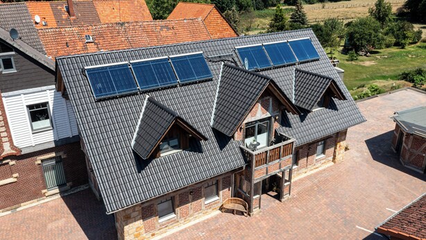 Um edifício de dois andares com telhado inclinado, painéis solares e fachada de tijolos.
