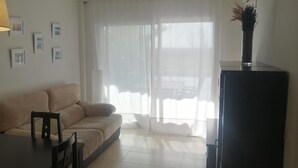 Uma sala de estar com um sofá bege, uma mesa de jantar com cadeiras, um abajur e um armário.