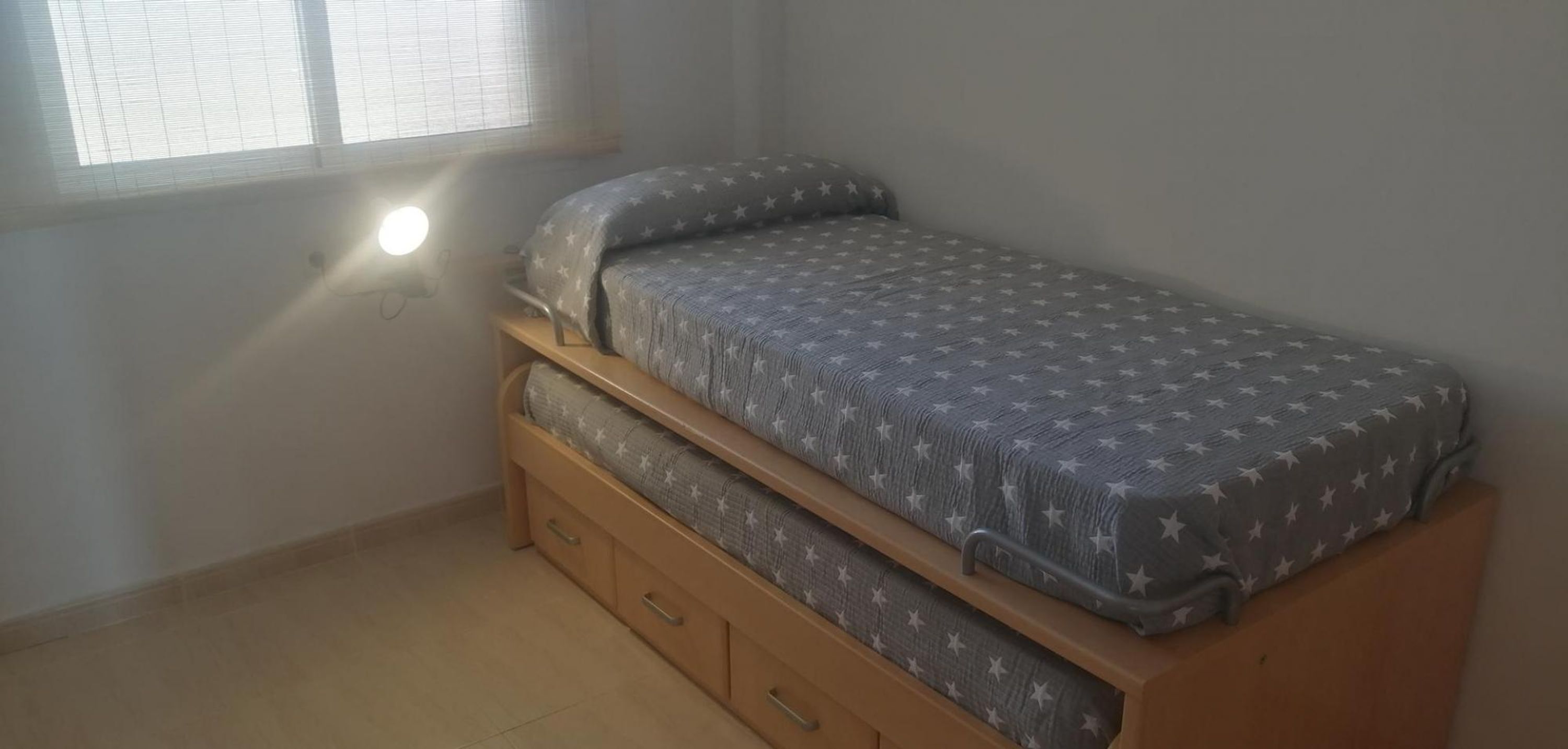 Uma cama de solteiro com um edredom estampado com estrelas, uma mesinha de cabeceira e um armário com gavetas.