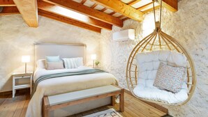 Um quarto aconchegante com teto de madeira, uma cadeira suspensa, uma cama com almofadas e uma mesa de cabeceira com abajur.