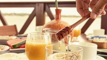 Uma mesa de jantar com um copo de suco de laranja, um copo de bebida branca com granola e um aplicador de mel.