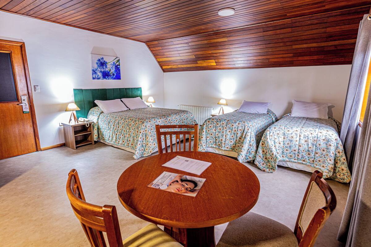 Quarto com duas camas, teto de madeira, mesa de jantar redonda e uma cadeira.