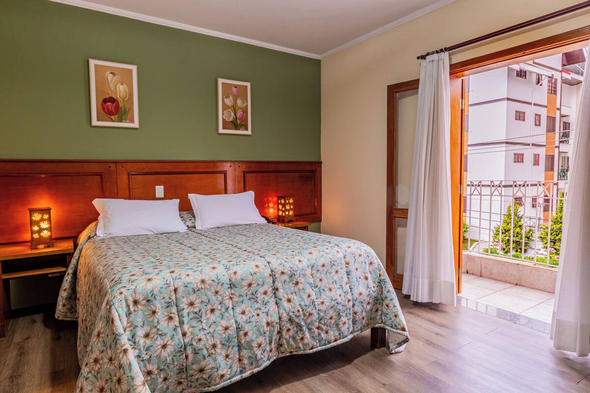 Um quarto com cama, duas mesas de cabeceira, cabeceira de madeira e varanda com vista para edifícios.