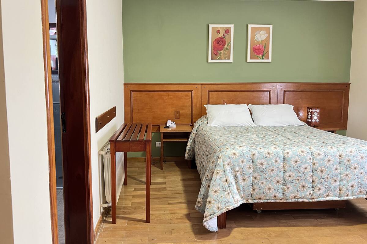 Quarto com cama de madeira, mesa de cabeceira e radiador.