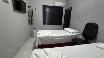 Quarto pequeno e limpo, com duas camas, televisão, ar condicionado e porta.