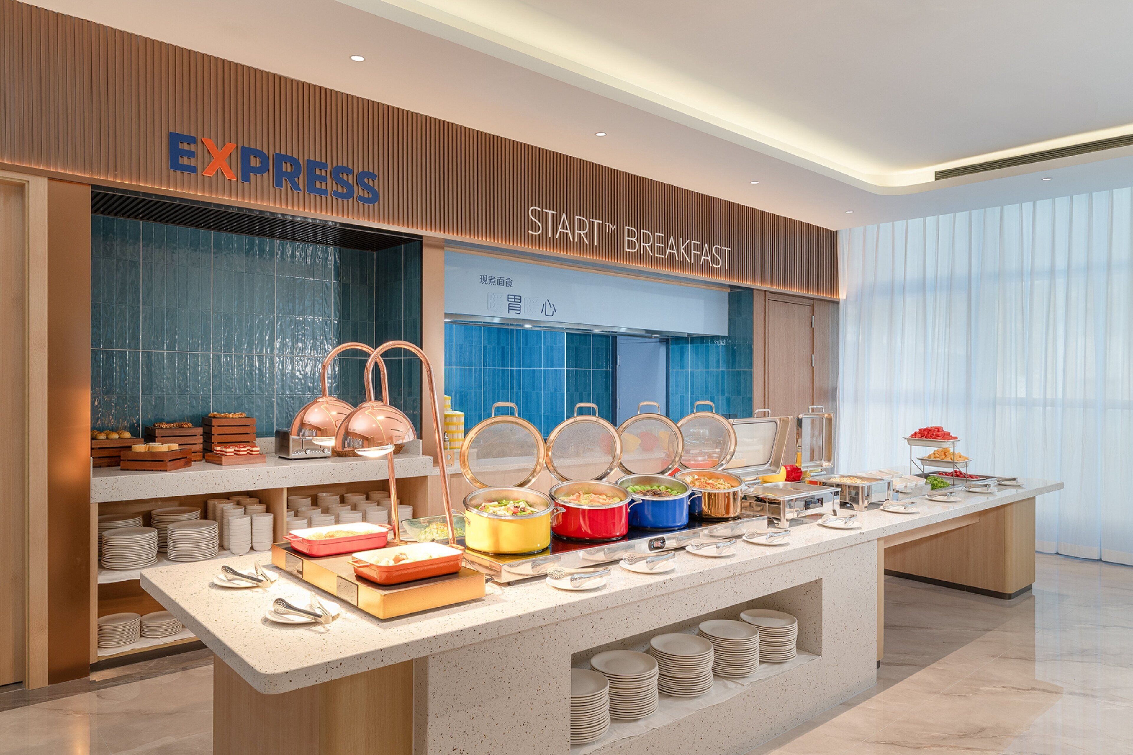Disposição de buffet com diversos recipientes de comida e utensílios, um letreiro com a inscrição 