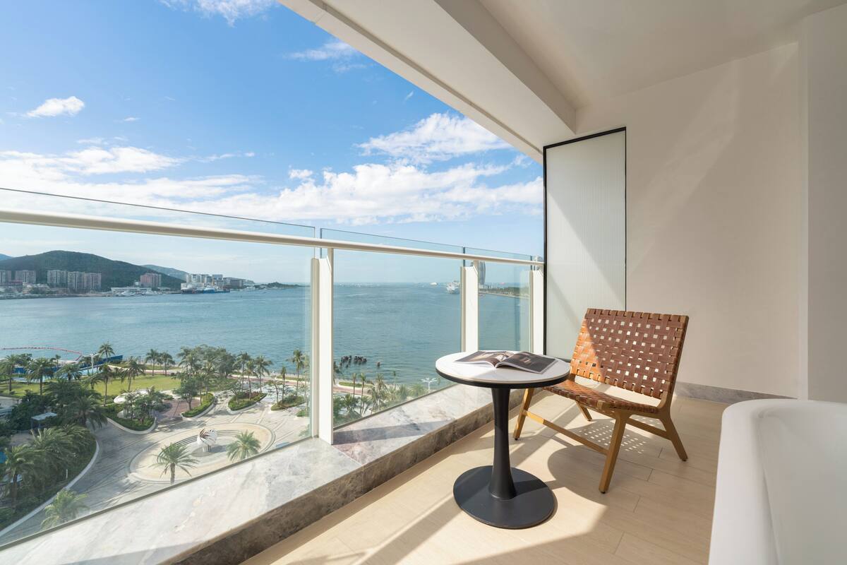 Uma varanda com vista para o mar, uma mesa com cadeira e um sofá branco.