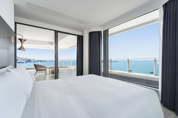 Quarto de hotel com uma cama grande, uma cadeira, vista para o mar e varanda.
