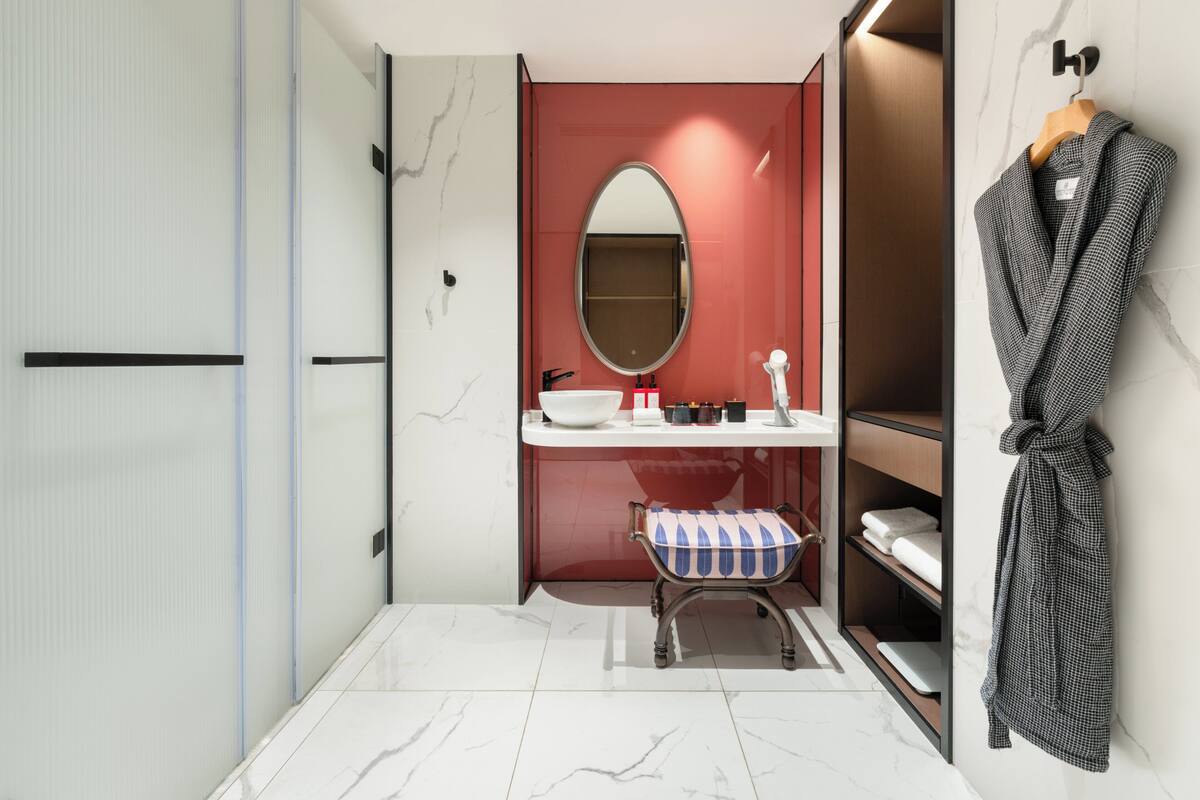 Uma casa de banho moderna com soalho de mármore, um espelho redondo, uma sanita branca e uma parede com detalhe em vermelho.