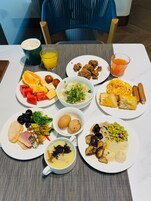 Uma mesa com diversos itens de pequeno-almoço, incluindo frutas, ovos, salsichas e uma tigela de sopa.