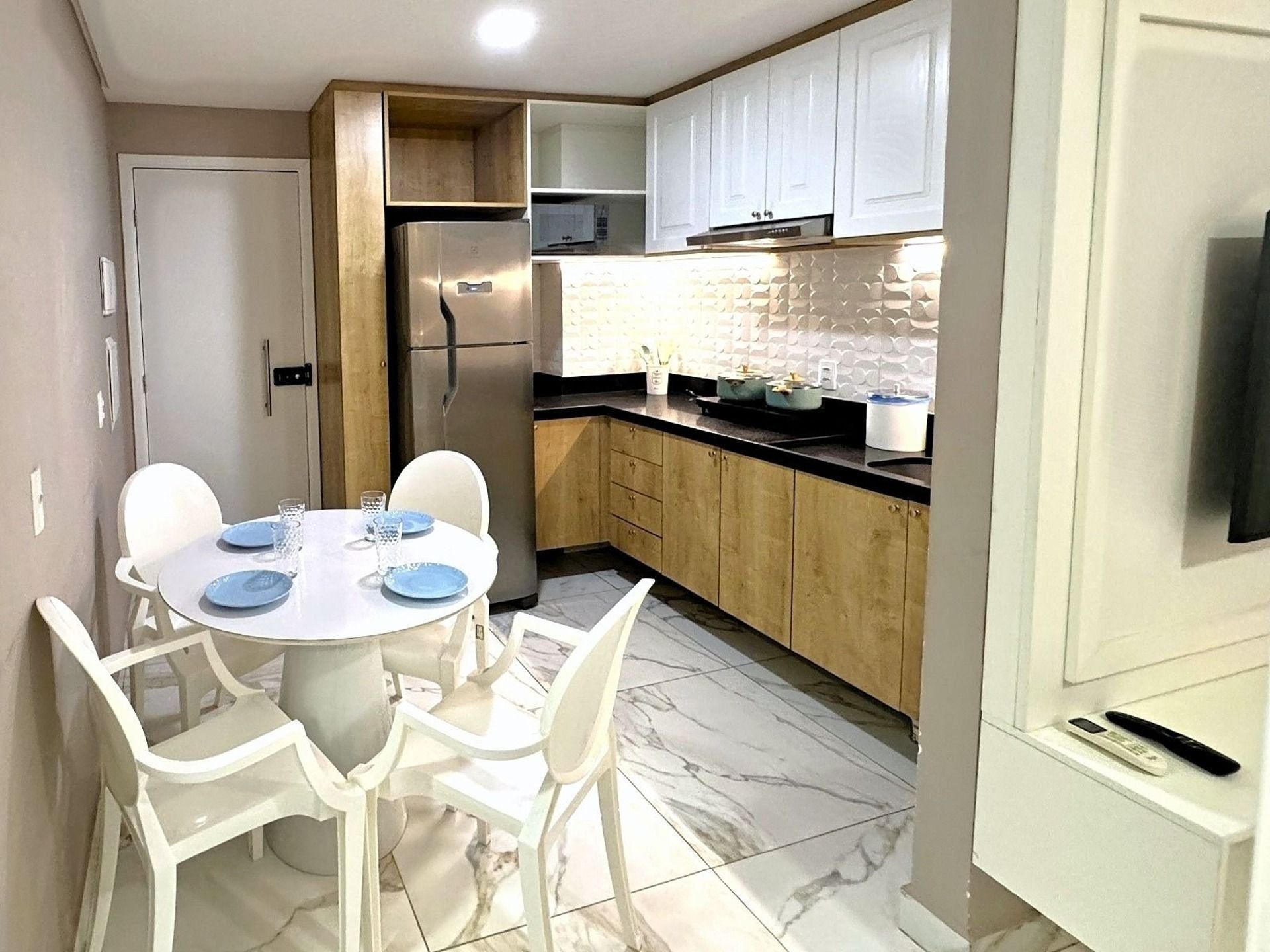 Cozinha compacta com armários brancos, micro-ondas embutido e geladeira de aço inoxidável.