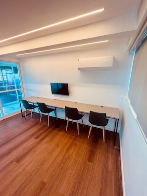 Um espaço de escritório moderno com uma mesa comprida, quatro cadeiras, uma TV de tela plana e um ar-condicionado na parede.