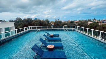 Piscina no terraço com cadeiras de descanso azuis e guarda-corpo de vidro.