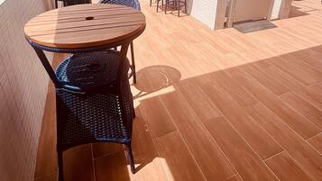 Terraço no telhado com mesa e cadeiras de madeira, área acessível para cadeiras de rodas e vista para o mar.
