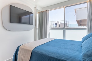 Quarto de hotel com cama, televisão montada e uma janela grande com vista para o exterior.